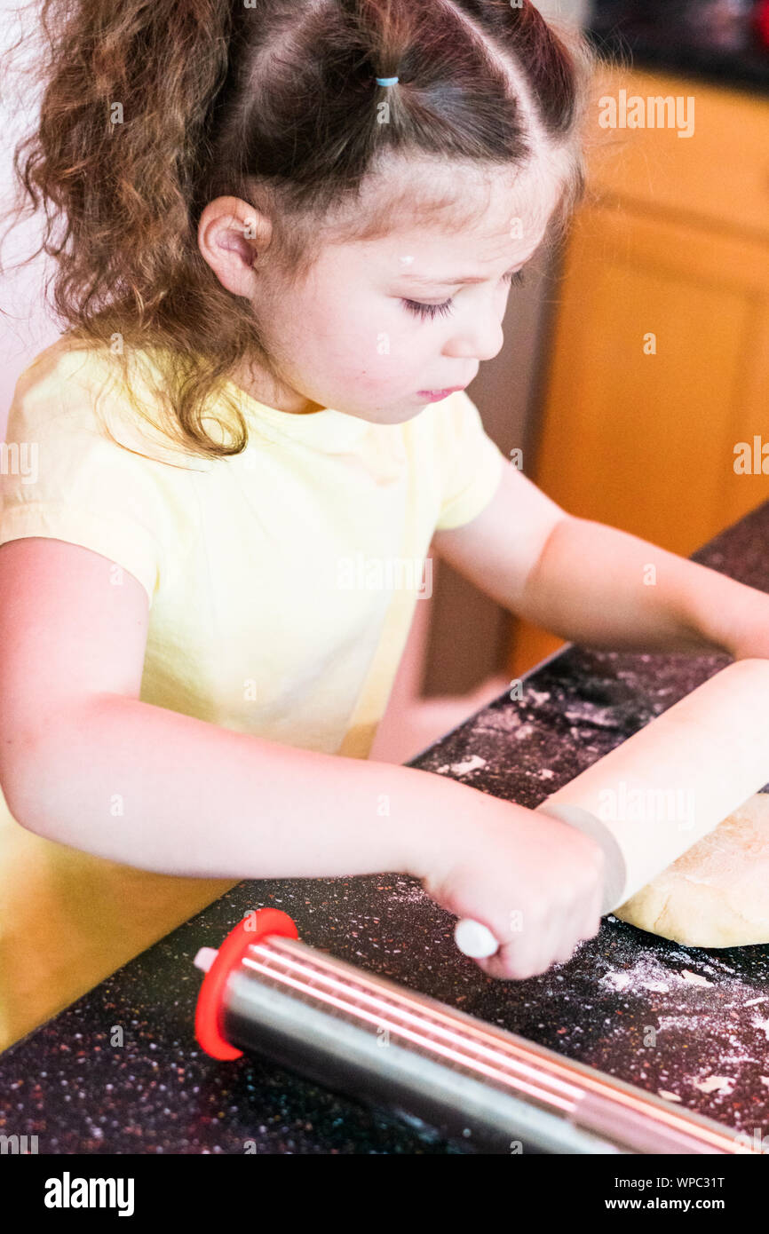Little girl rolling sugar cookie dough with a little rolling pin on the ...