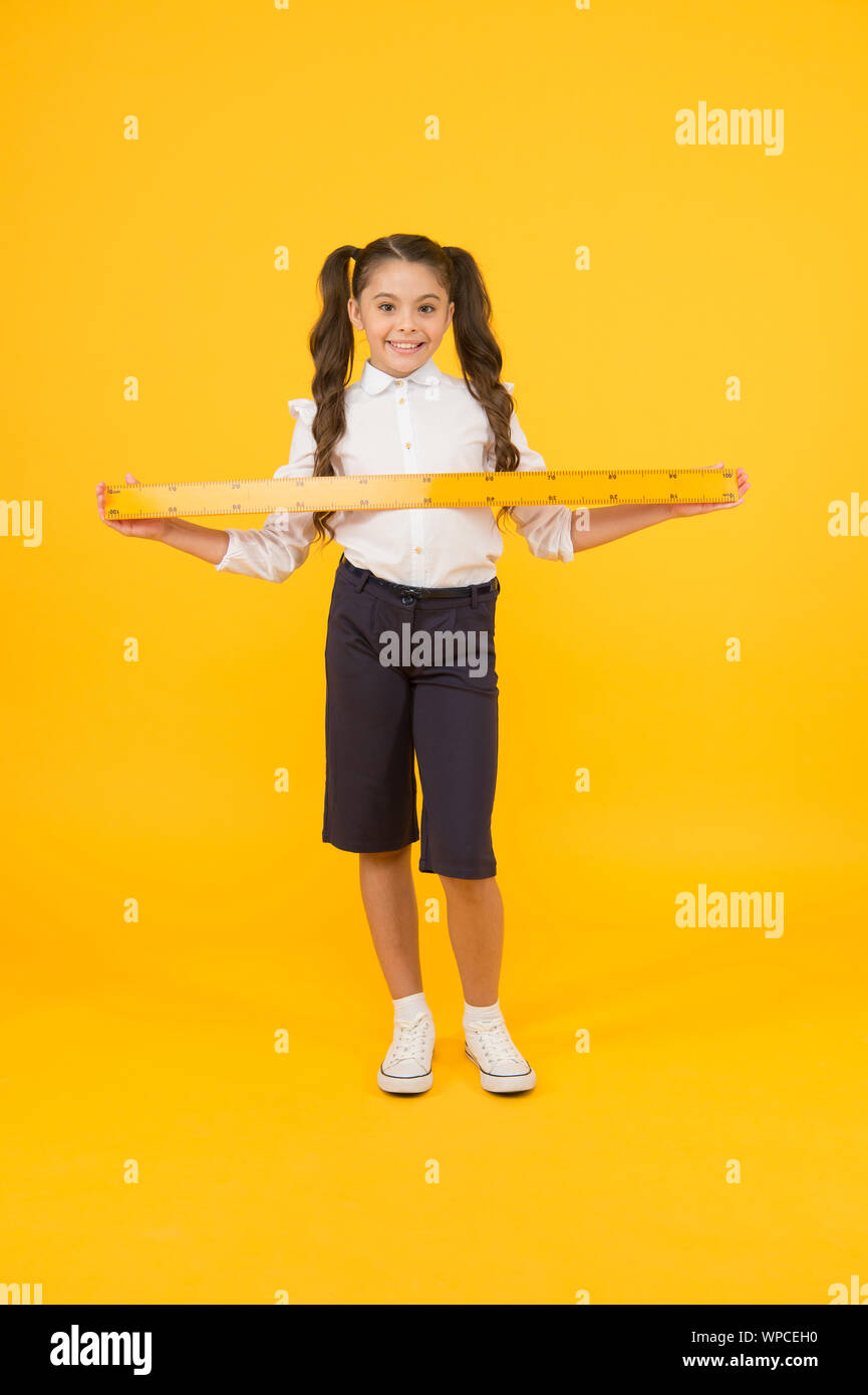 Measuring length. Little girl holding metric ruler on yellow background ...