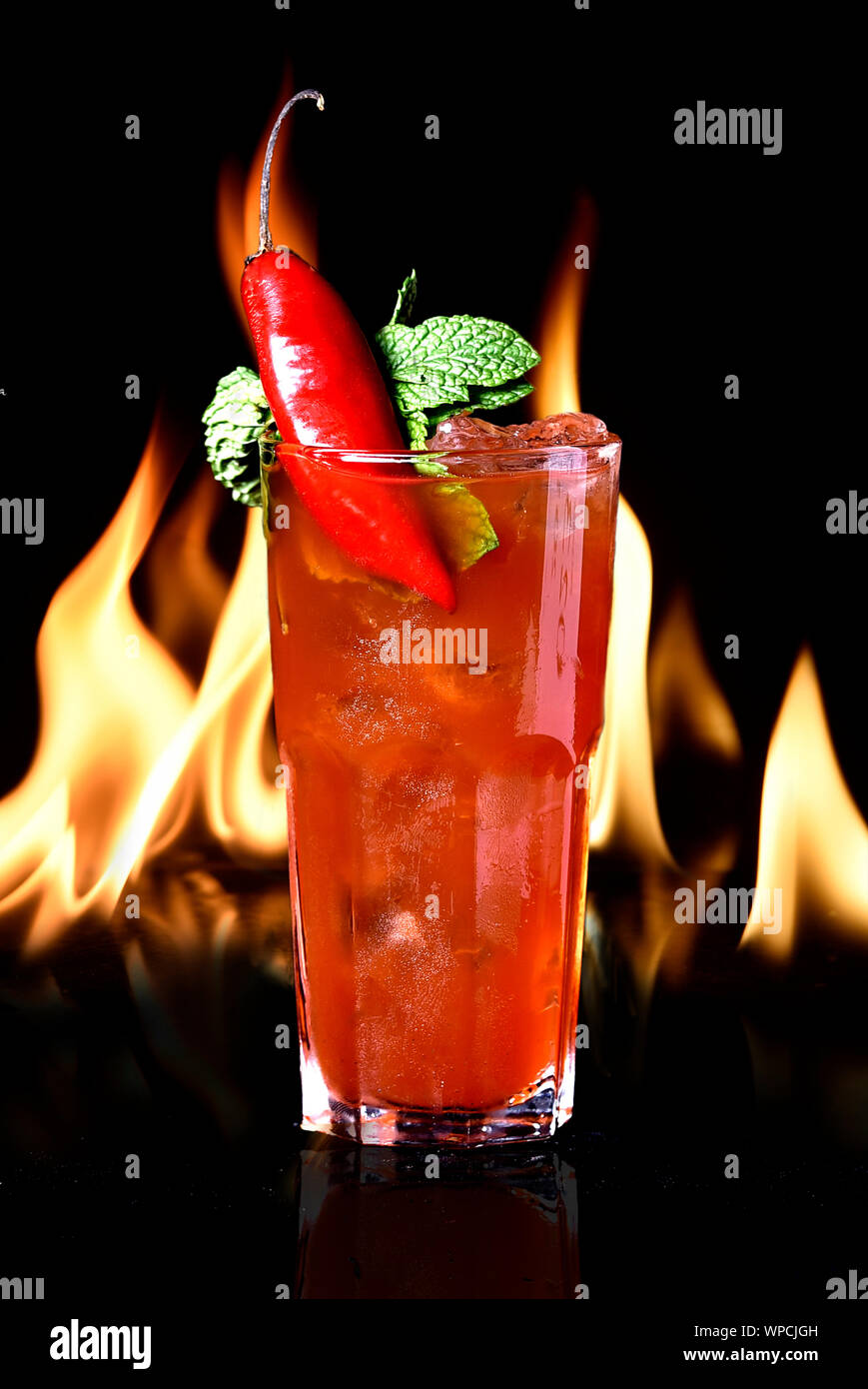 exotic red drink with fire behind and reflection on black background ...