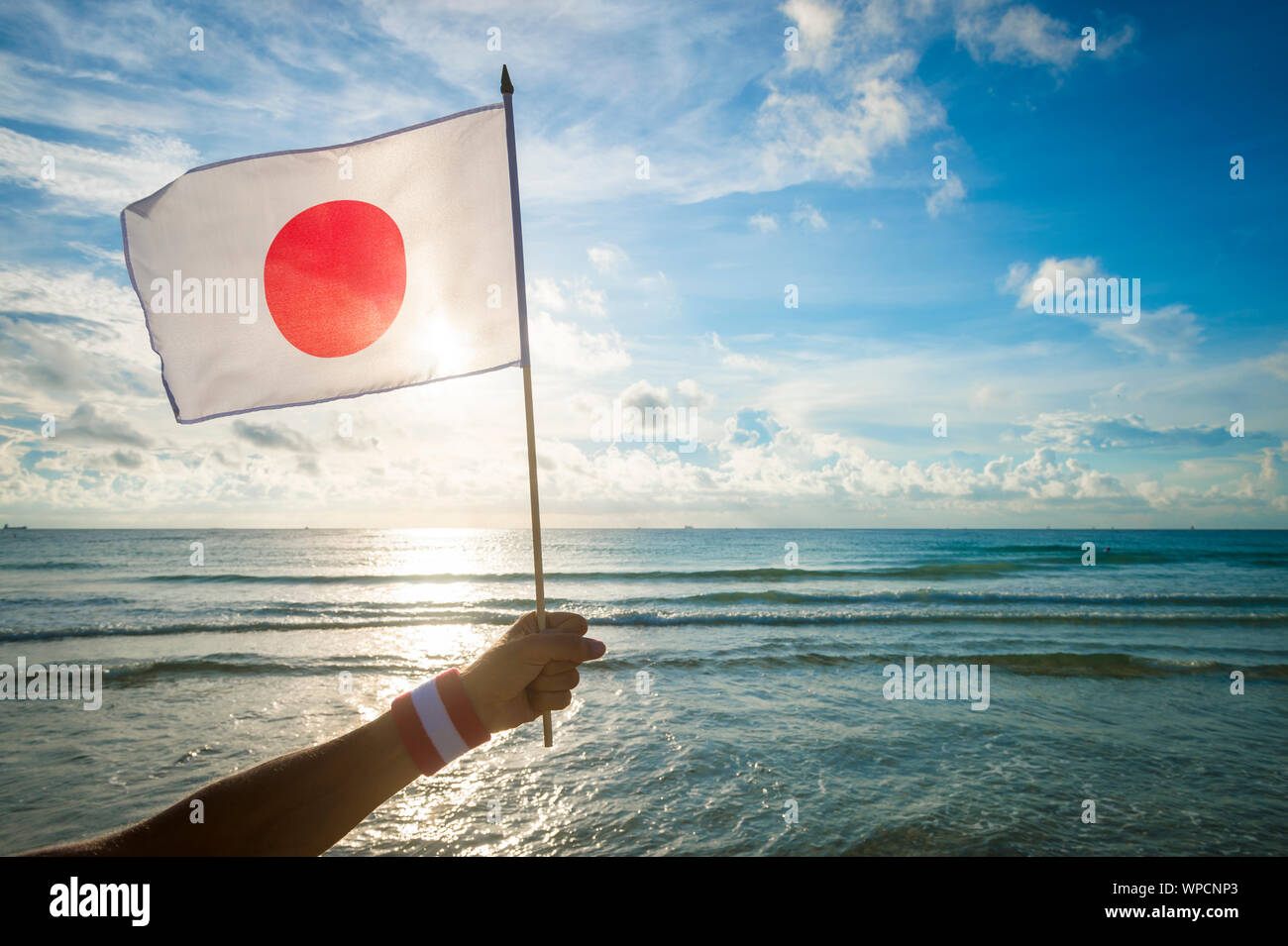 Hand with Japan red and white wristband holding a Japanese flag waving ...