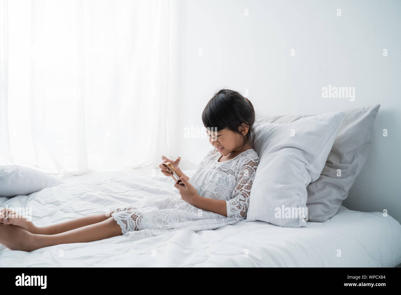 asian girl child using mobile phone on bed Stock Photo - Alamy