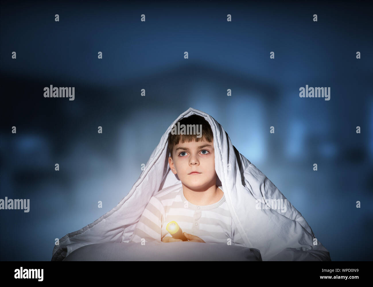 Serious child with flashlight hiding under blanket. Attentive kid lying ...