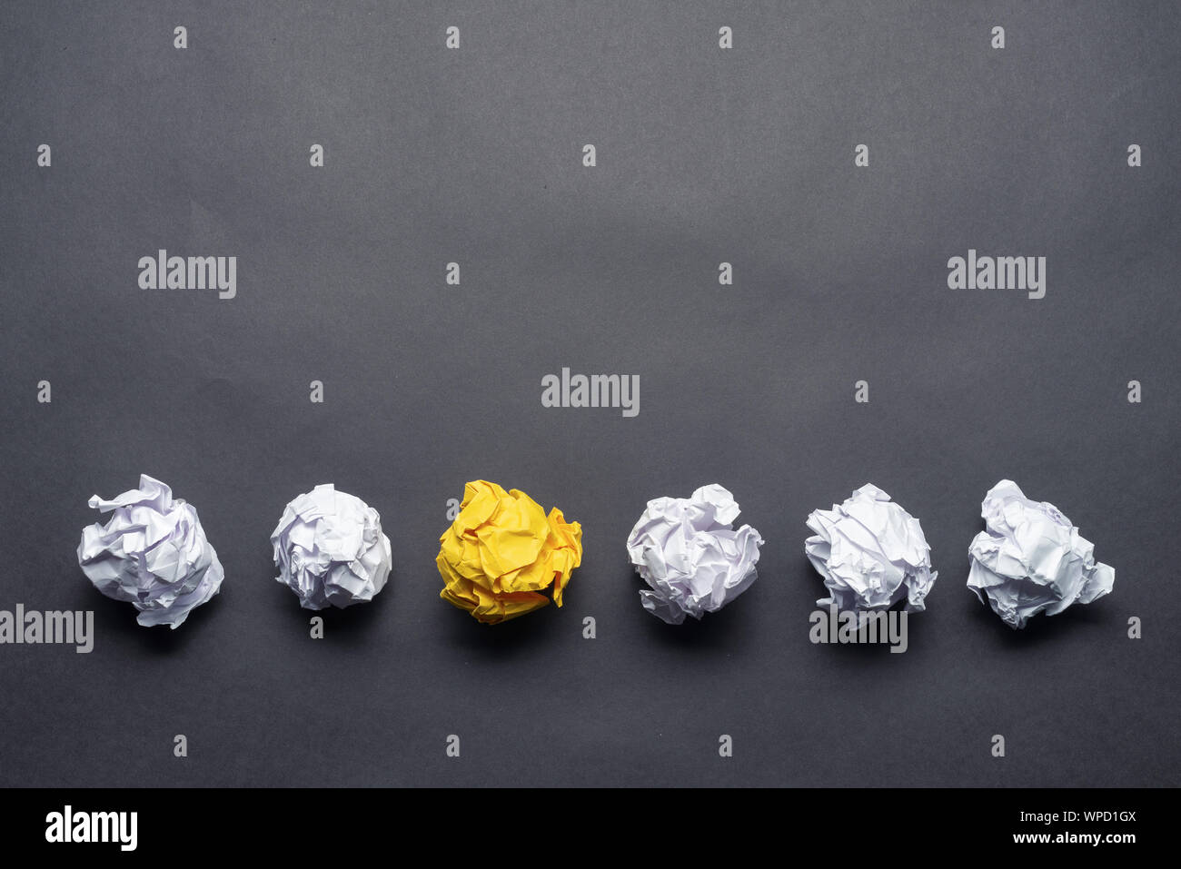 Crumpled yellow paper ball among white balls on black background ...