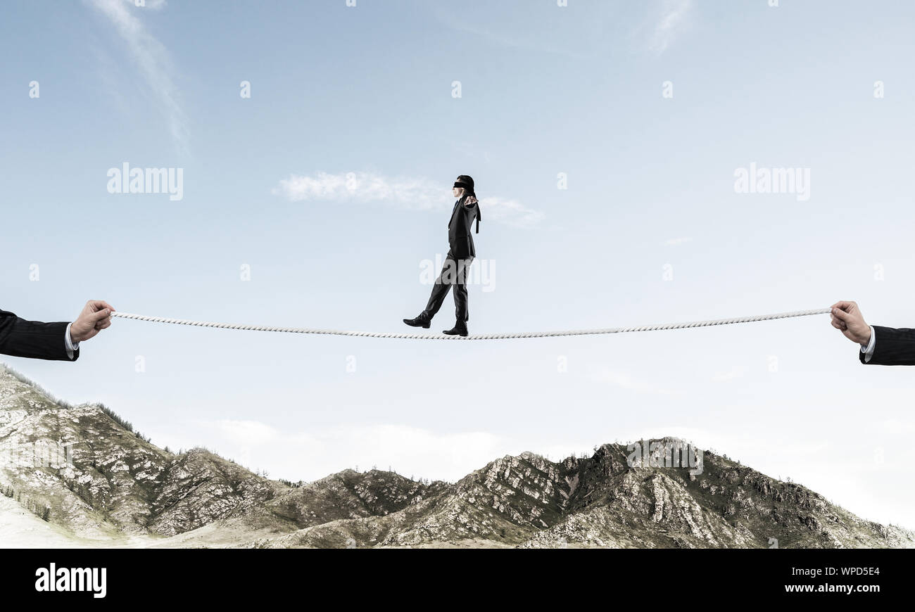 Businessman walking blindfolded on rope above high mountains as symbol ...