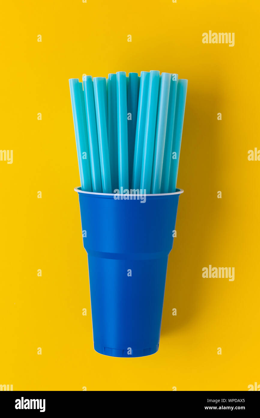 Dark blue plastic single use cup on yellow background. Many drinking ...