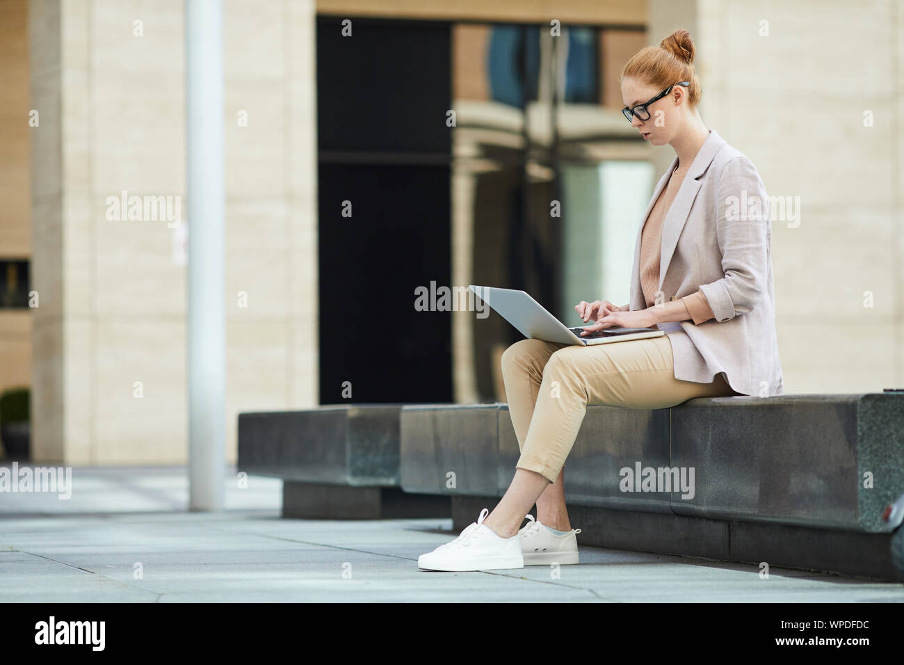 Side view portrait of red haired young woman using laptop outdoors ...