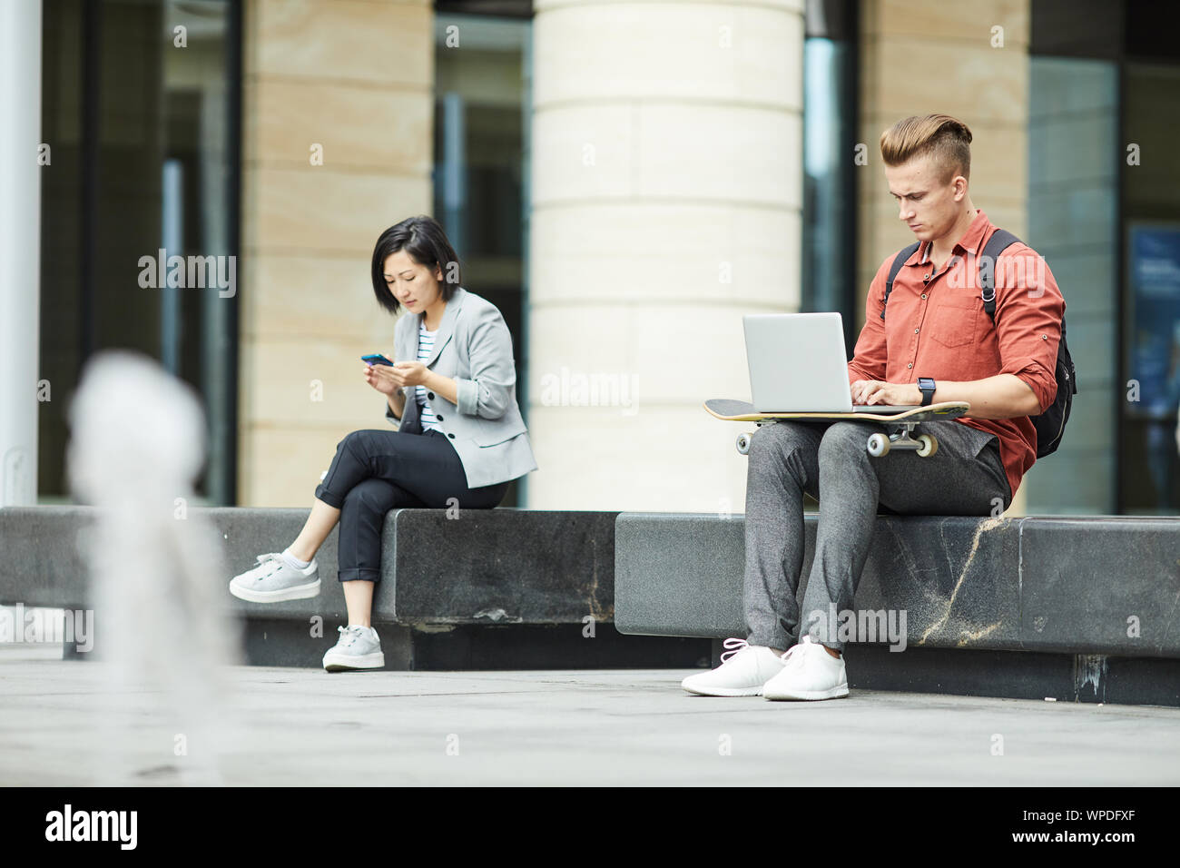 Full length portrait of two young people using electronic devices while ...