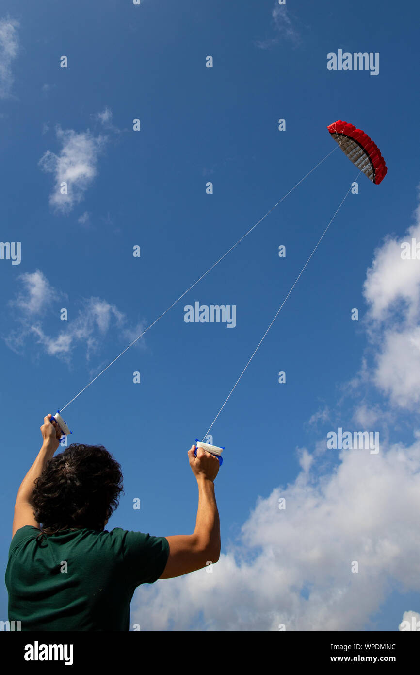 Young man, back view, controlling a red kite with blue sky in the ...