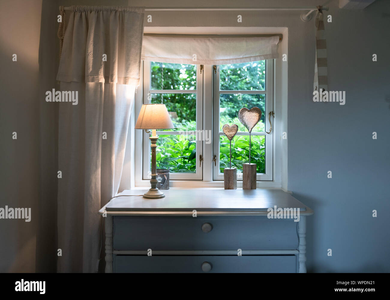 Window inside country house with lamp and heart decoration on chest of ...