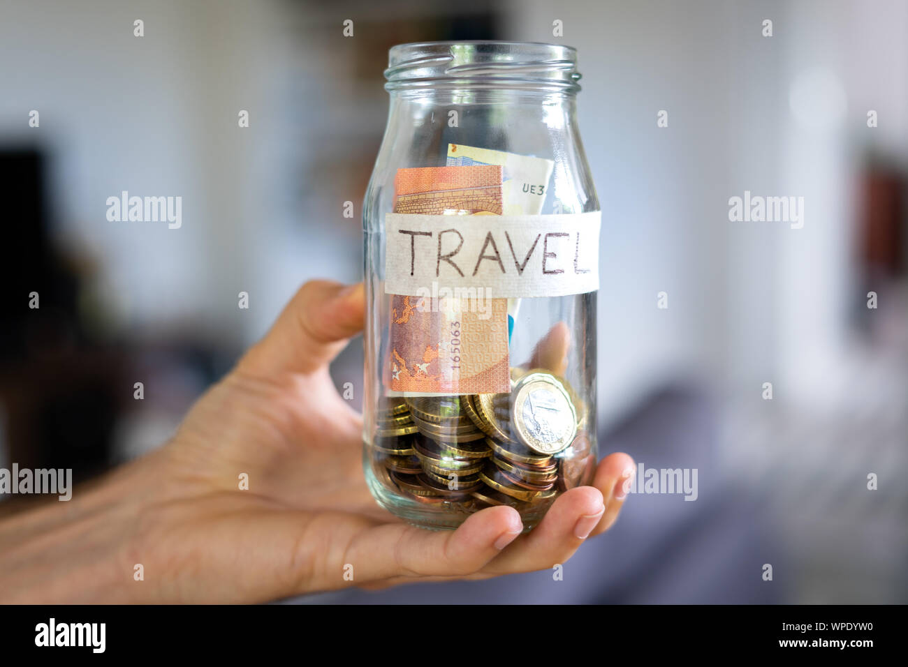 Man's hand holding a jar with euro coins and notes and a handwritten ...