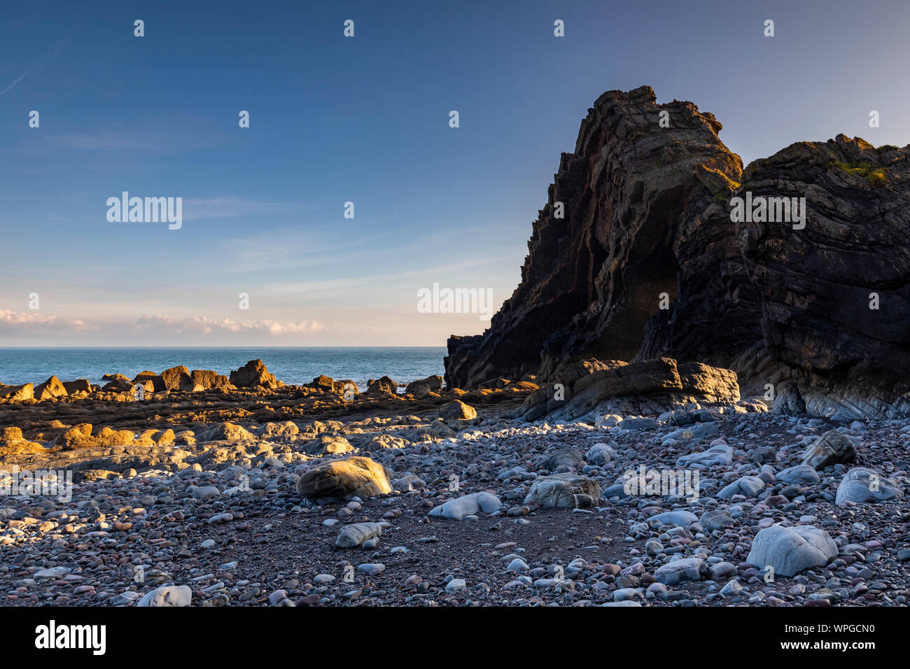 The morning sun shines through Blackchurch Rock at Mouthmill Beach on ...