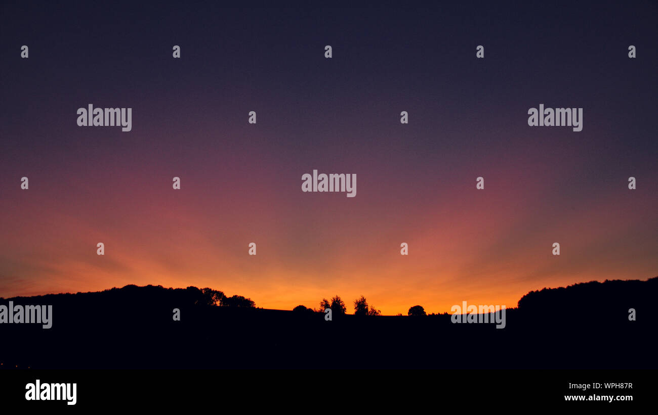 the sun setting behind a hill Stock Photo - Alamy