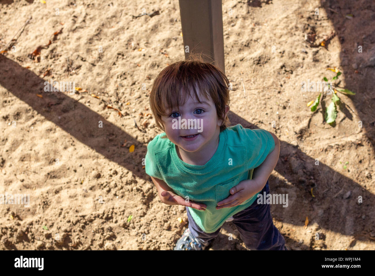 A toddler is seen from above as he stands in a sandbox in a public ...