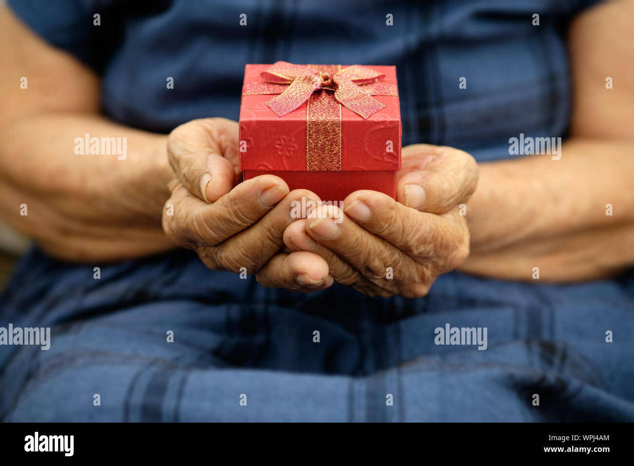 Wrinkled old hands holding little gift with red bow Stock Photo - Alamy