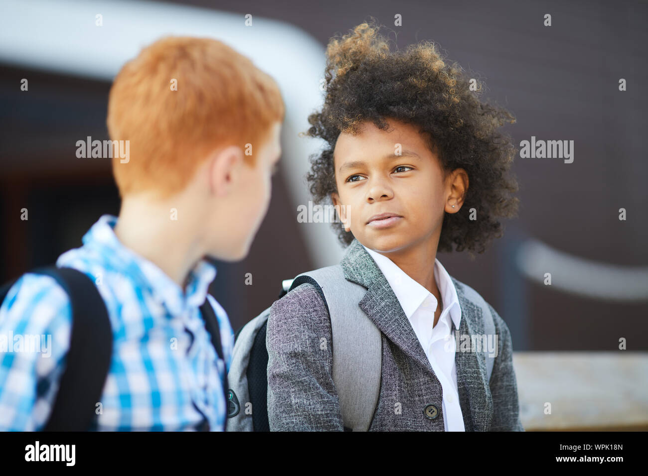 Little African boy talking to his friend while they standing outdoors ...
