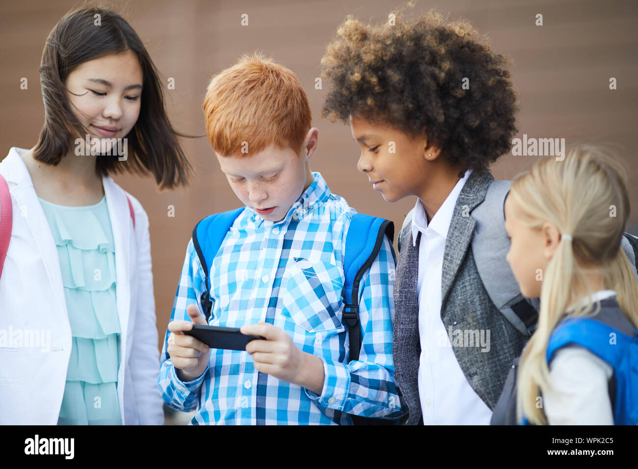 Schoolboy with backpack playing game on his mobile phone while standing ...