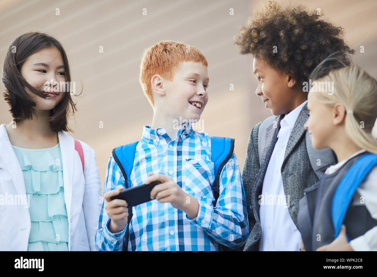 Red haired schoolboy with mobile phone talking to his classmates and ...