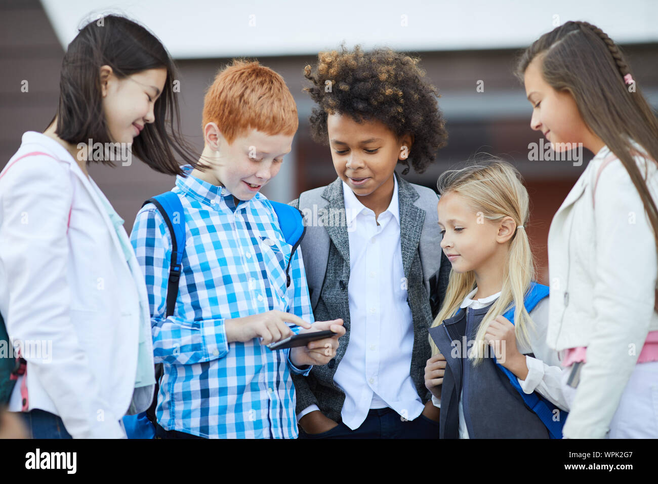 Group of classmates with backpacks standing together and looking at the ...