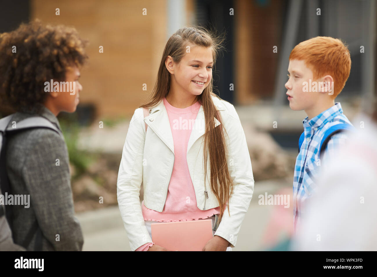 Smiling cute girl talking to her friends while they standing outdoors ...