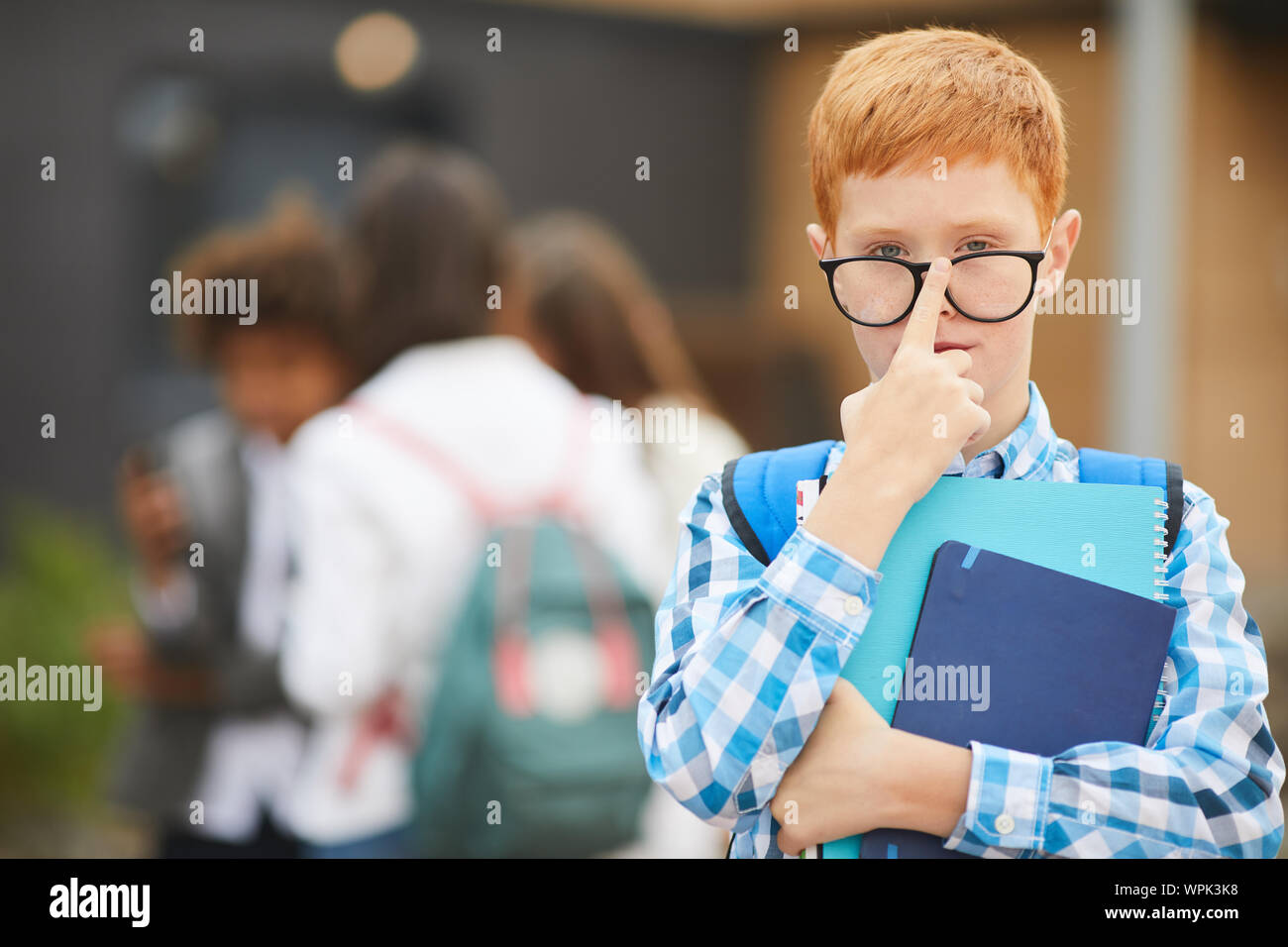 Portrait of red haired boy in eyeglasses holding books and looking at ...