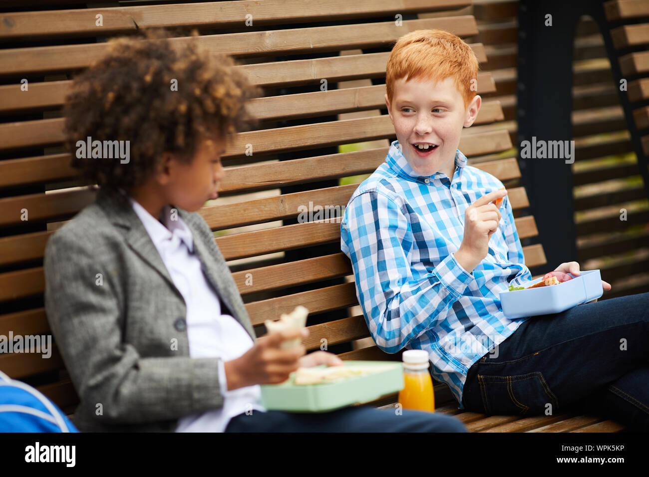 Two boys eating sandwiches and talking to each other while resting on ...