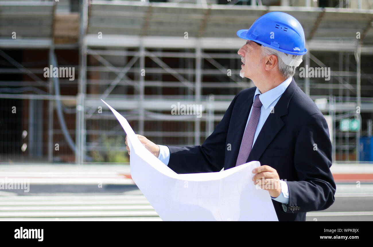 Senior engineer reading a blueprint i front of a construction site ...