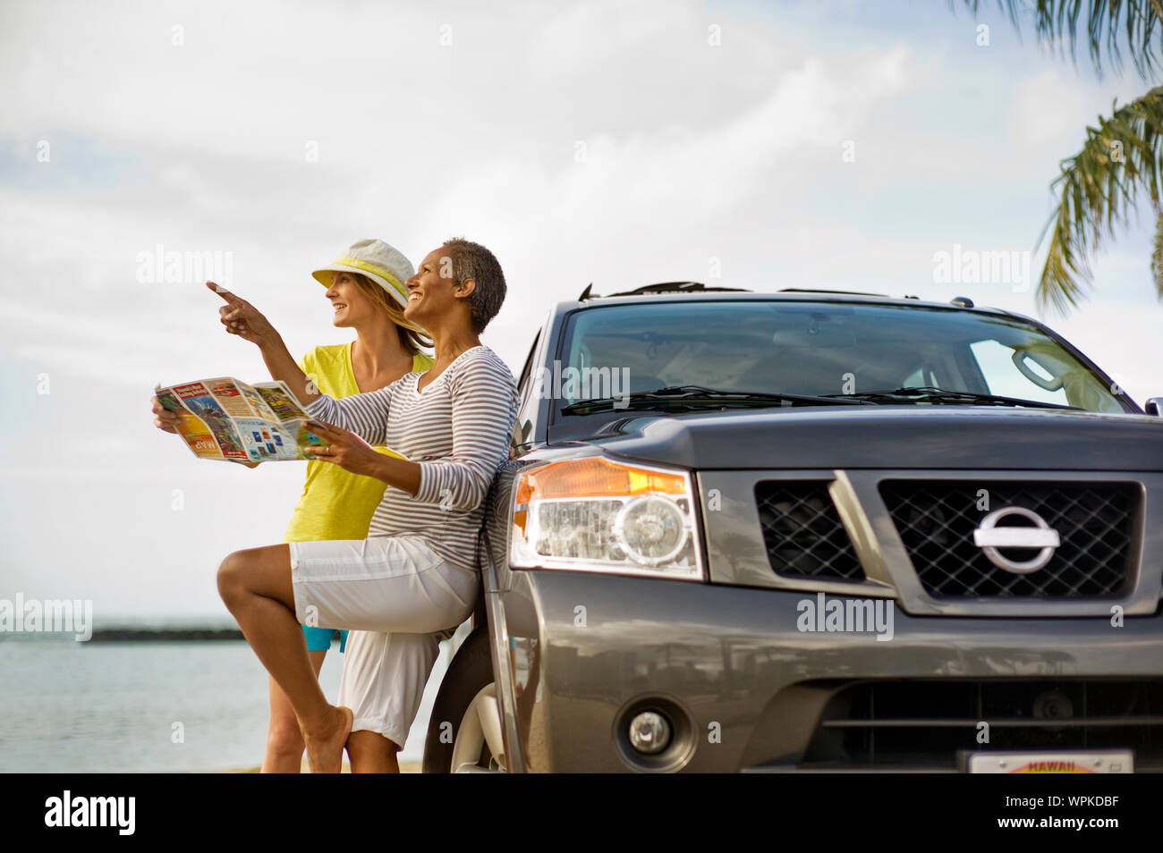 Two friends looking at map, leaning against car Stock Photo - Alamy