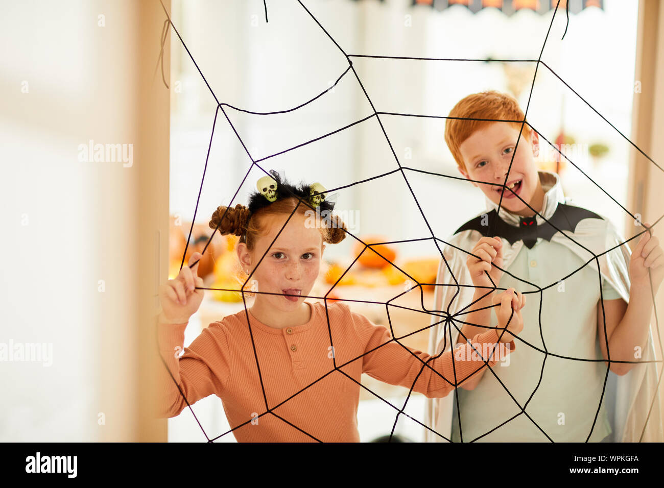 Portrait of two playful children in costumes standing behind the cobweb ...