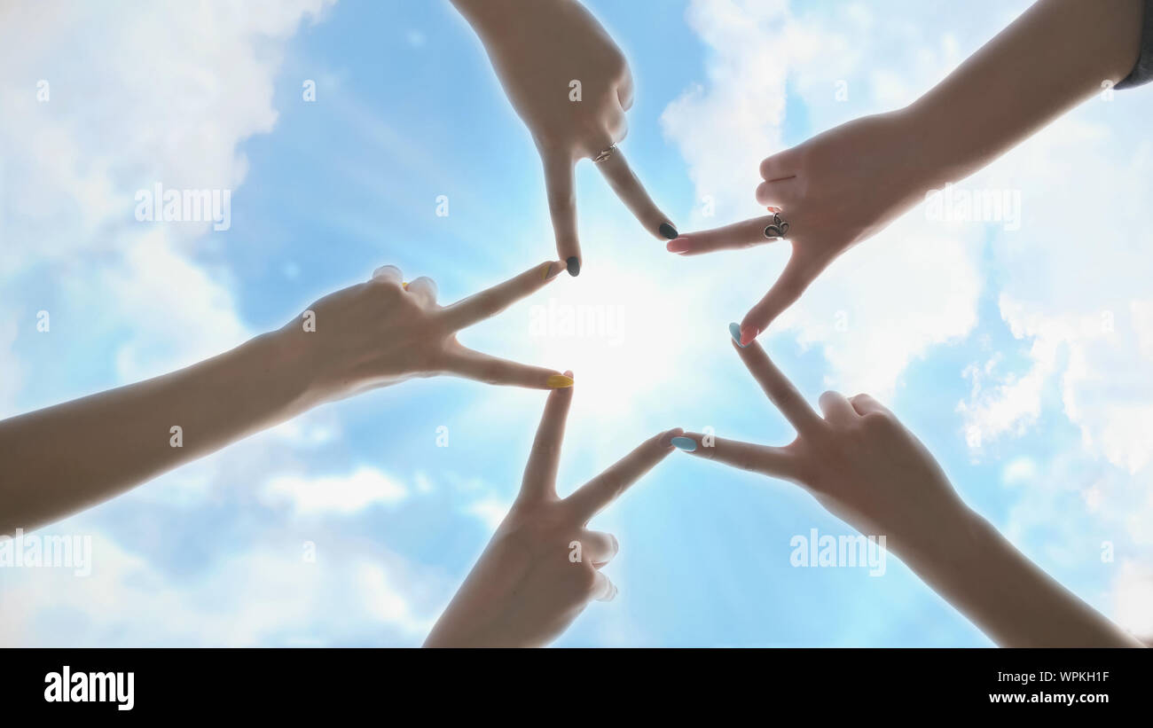 People forming star shape with their fingers against the blue sky with ...