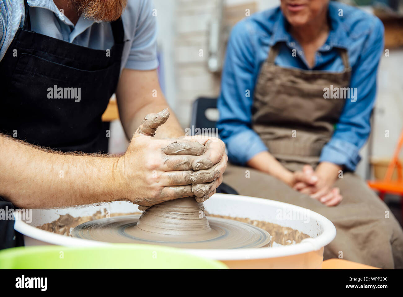 Senior woman spinning clay on a wheel with a help of a teacher at ...