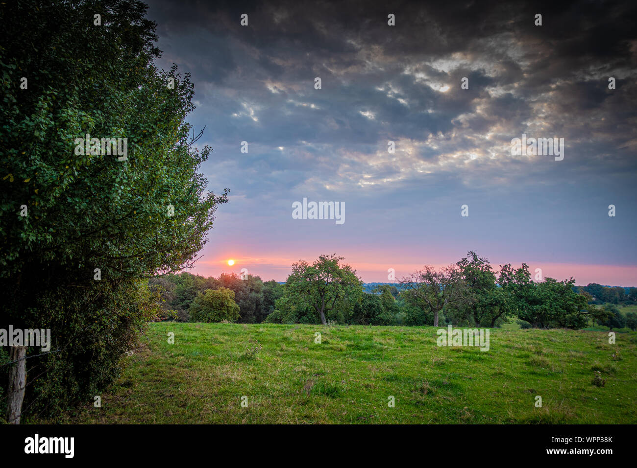 a beautiful coloured sunrise over a green meadow and on the other side ...