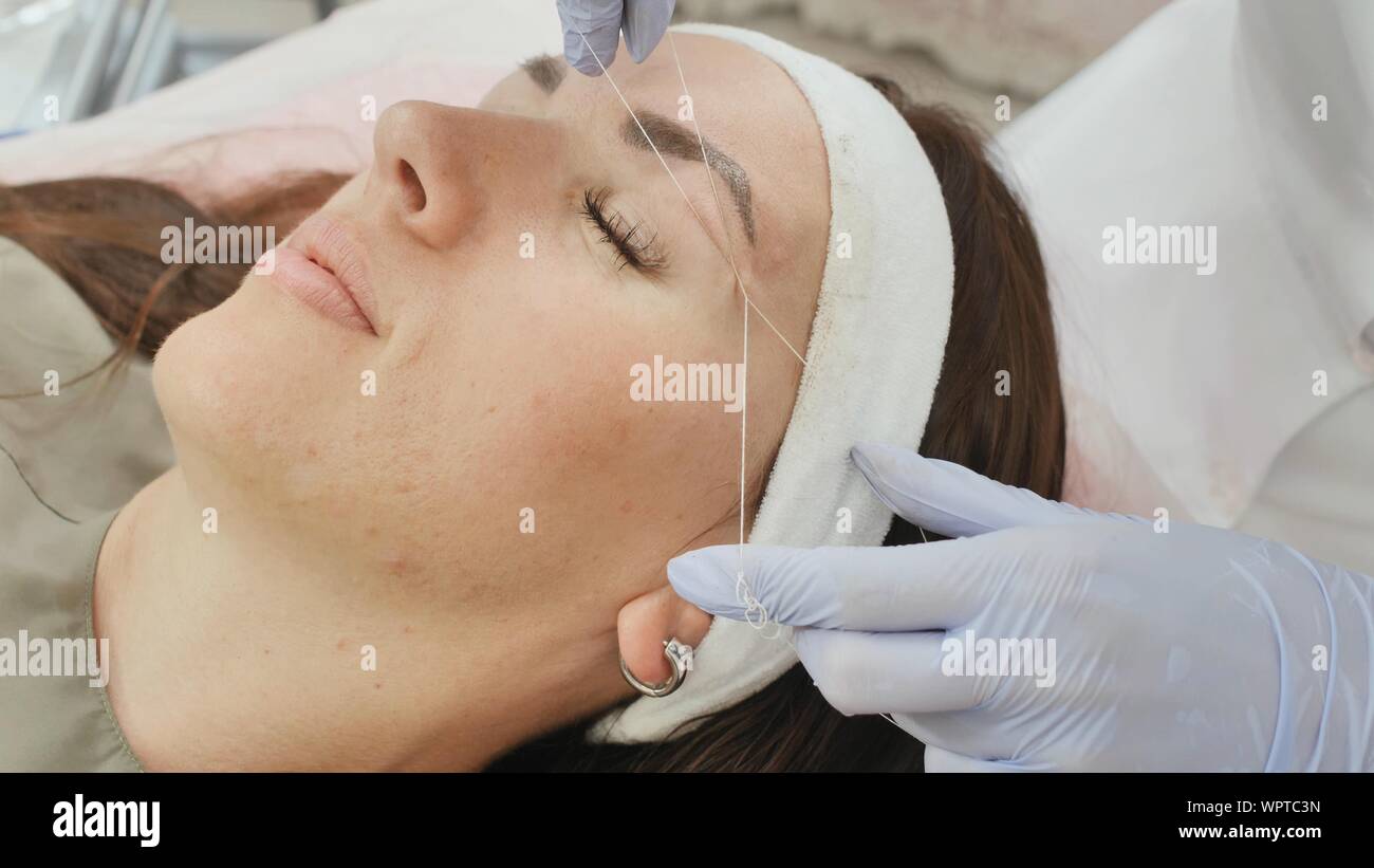 Closeup part of face depilation of eyebrows with a thread. Permanent ...