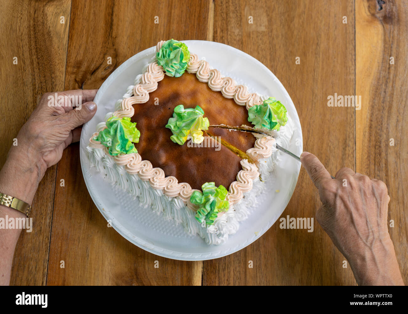 A cake on a table two wrinkled old hand, one cutting the cake and the ...