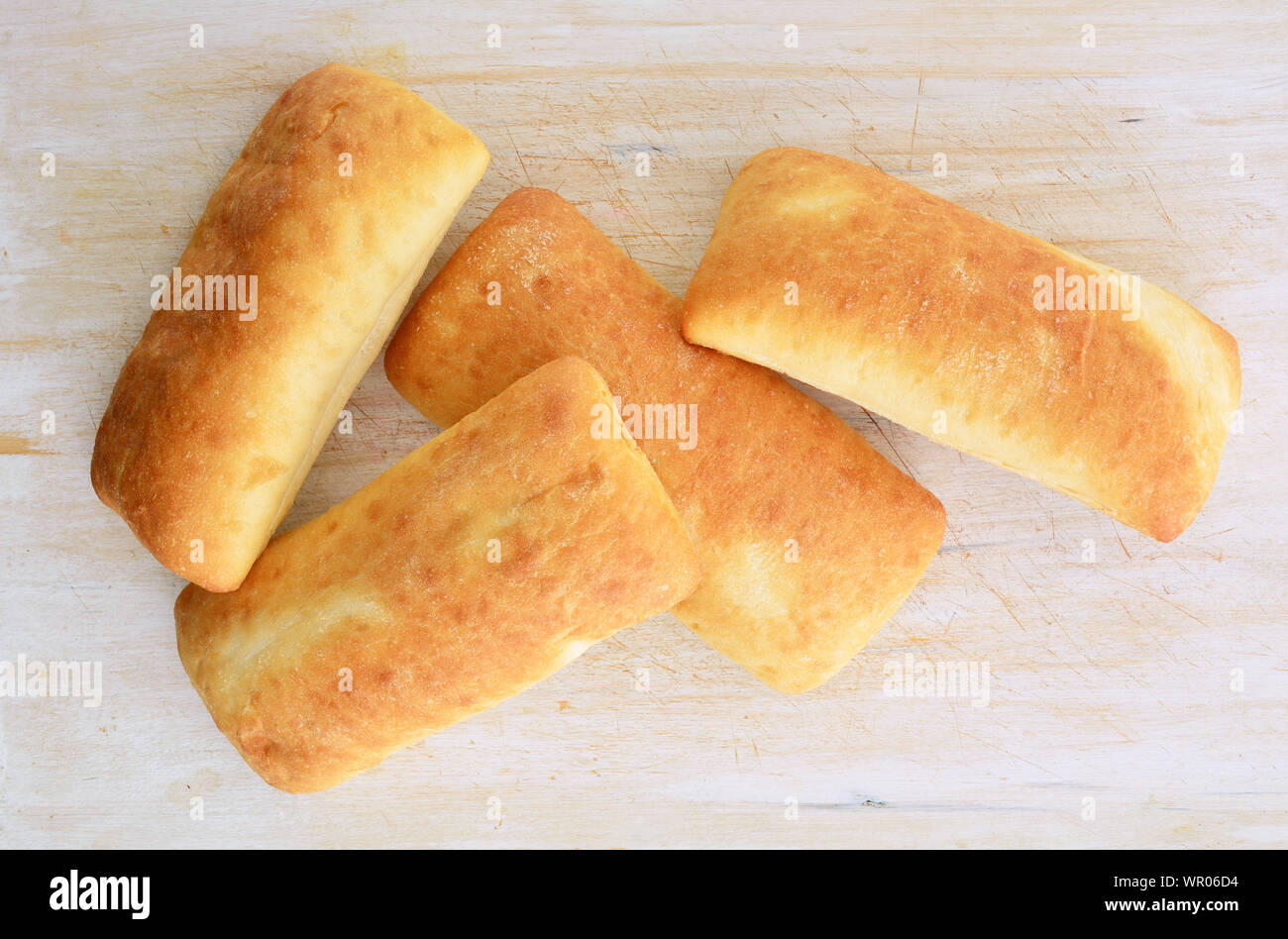 Fresh baked ciabatta sticks on well used white bread board in ...