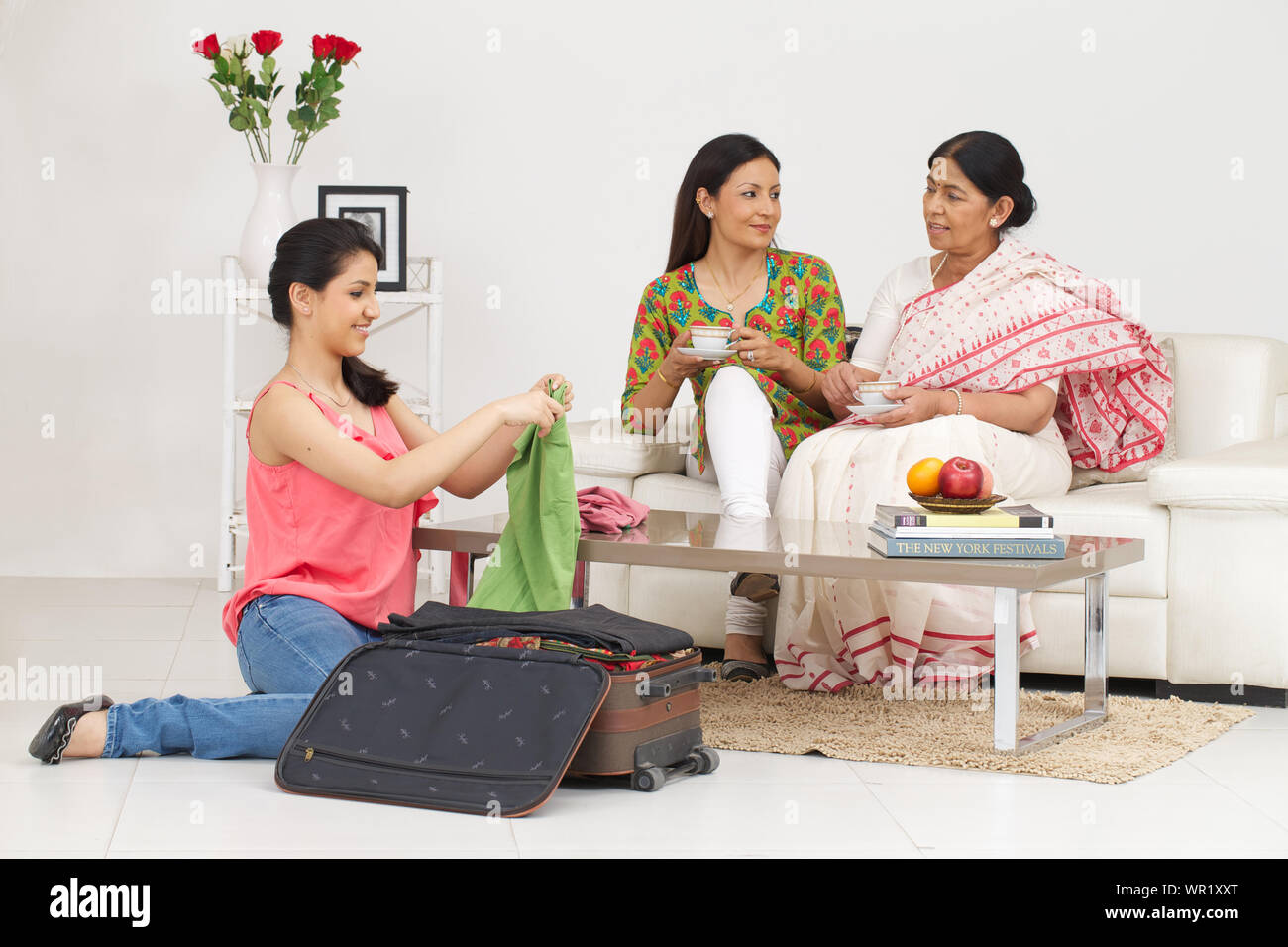 Young woman packing suitcase with her family in the background Stock ...