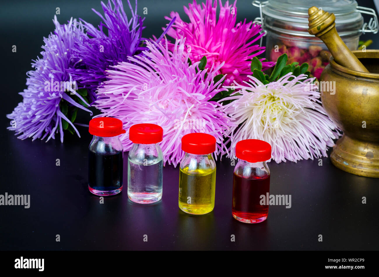 Glass bottles of essential oil with fresh flowers on black background ...