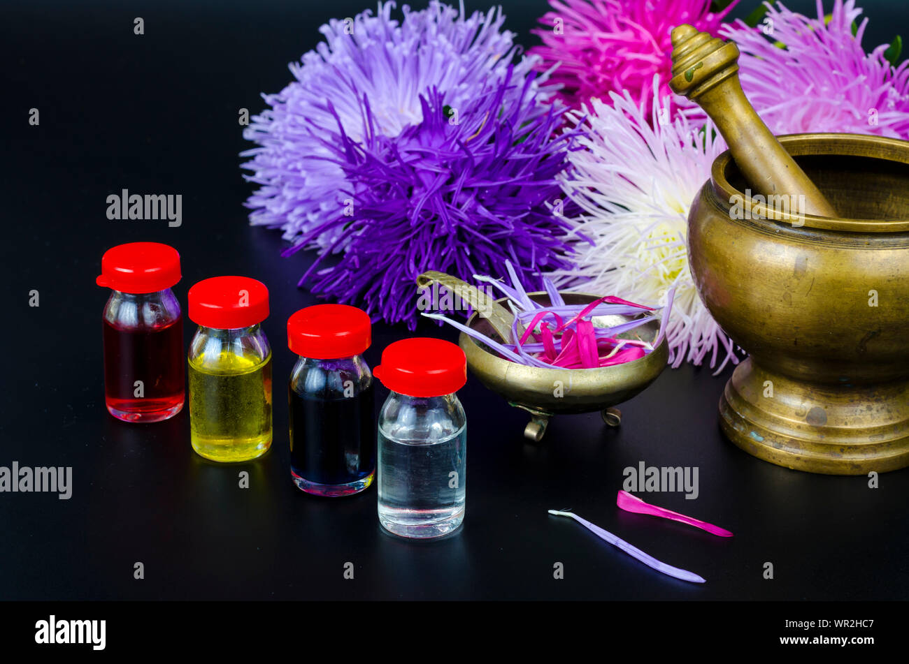 Glass bottles of essential oil with fresh flowers on black background ...