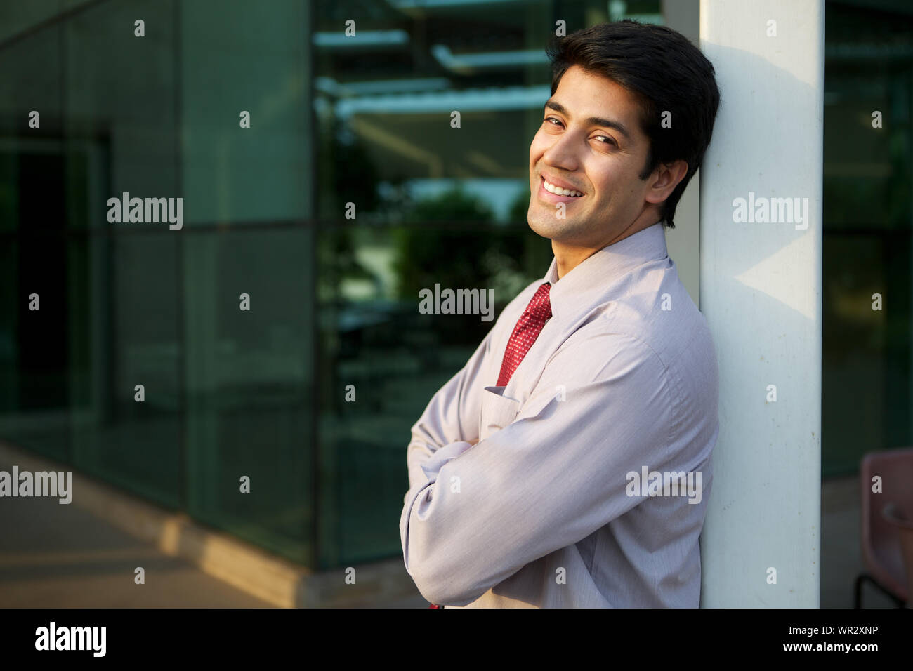 Businessman leaning against pole and smiling Stock Photo - Alamy