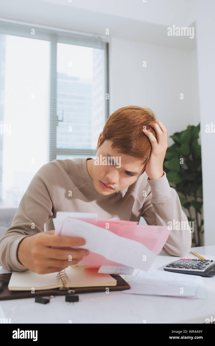 Asian young man counting using calculator and stress in problem with ...