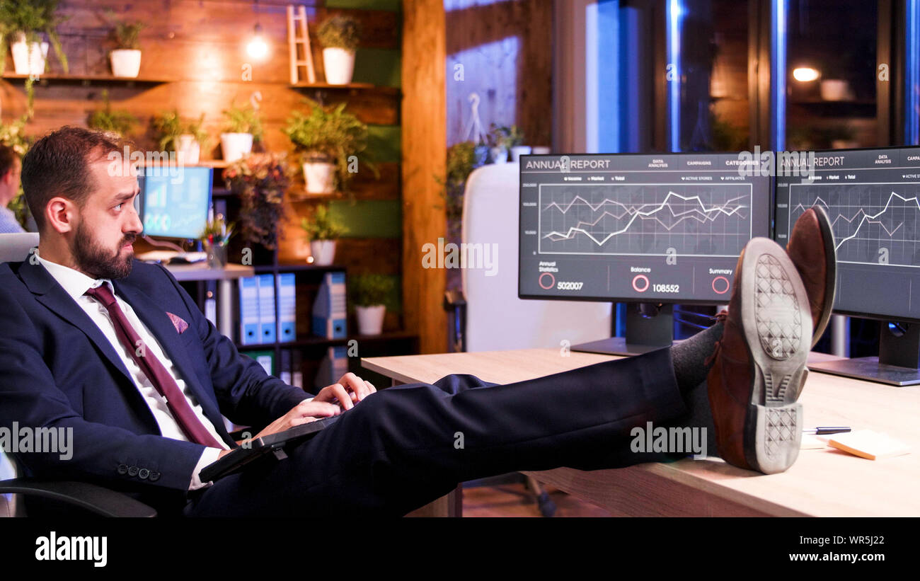 Manager working on graphs with feet on the table. Two screens Stock ...