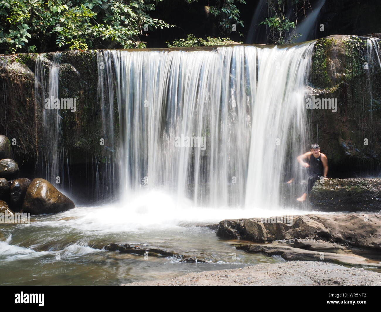 Man Sitting On Rock Under Waterfall Stock Photo - Alamy