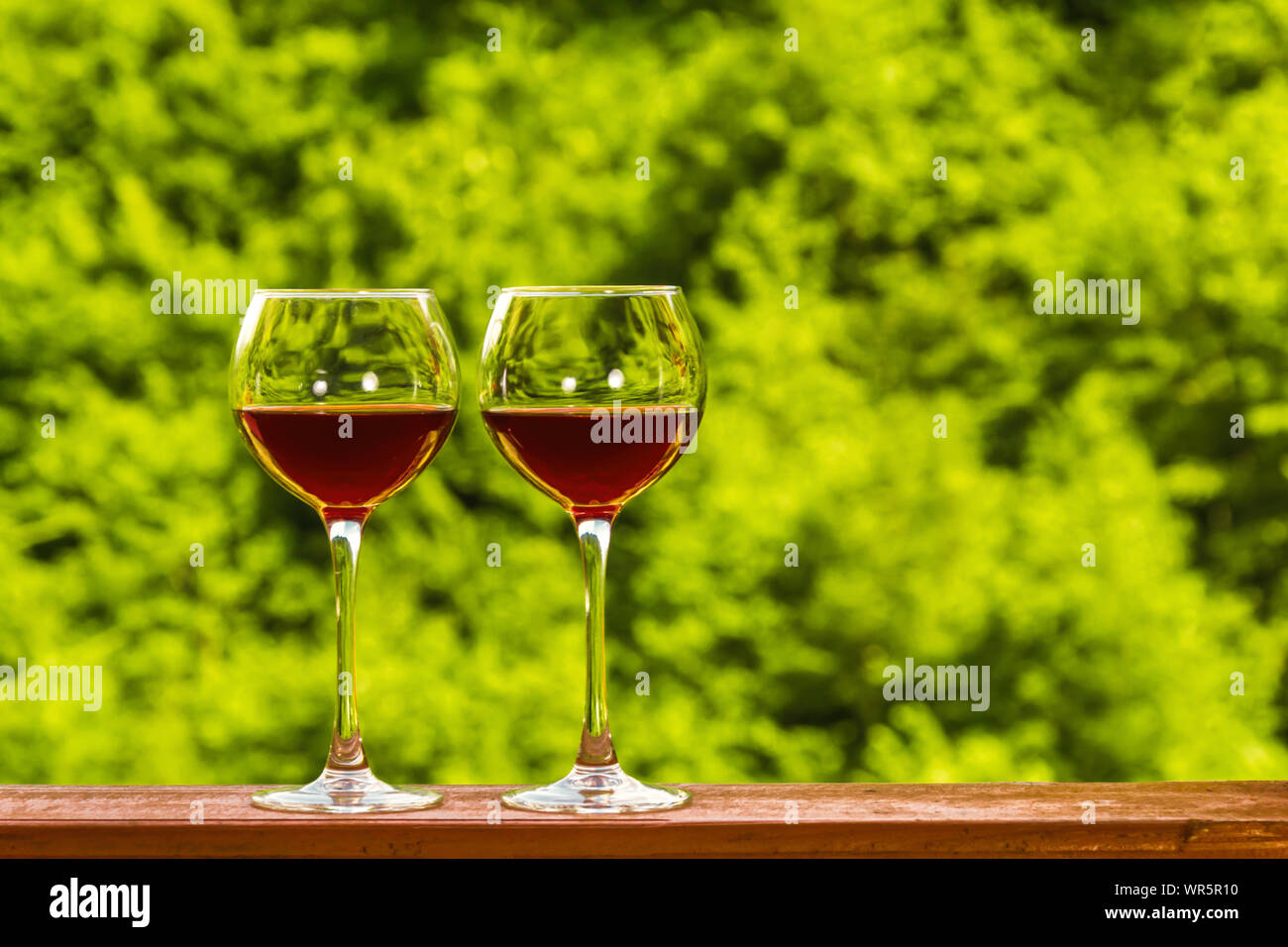 Two glasses of red wine on the deck of a wooden house on a green fresh ...