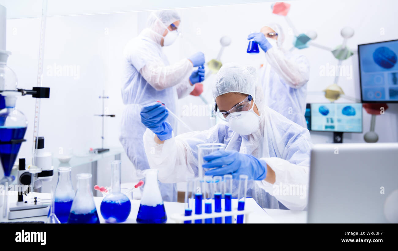 Three scientists analyzing several containers with blue liquid. High ...