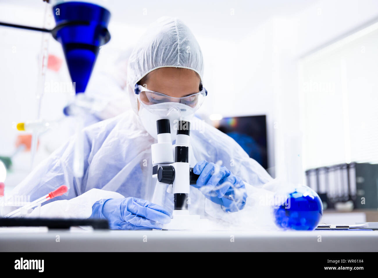 The researcher looks under the microscope near a beaker from which ...