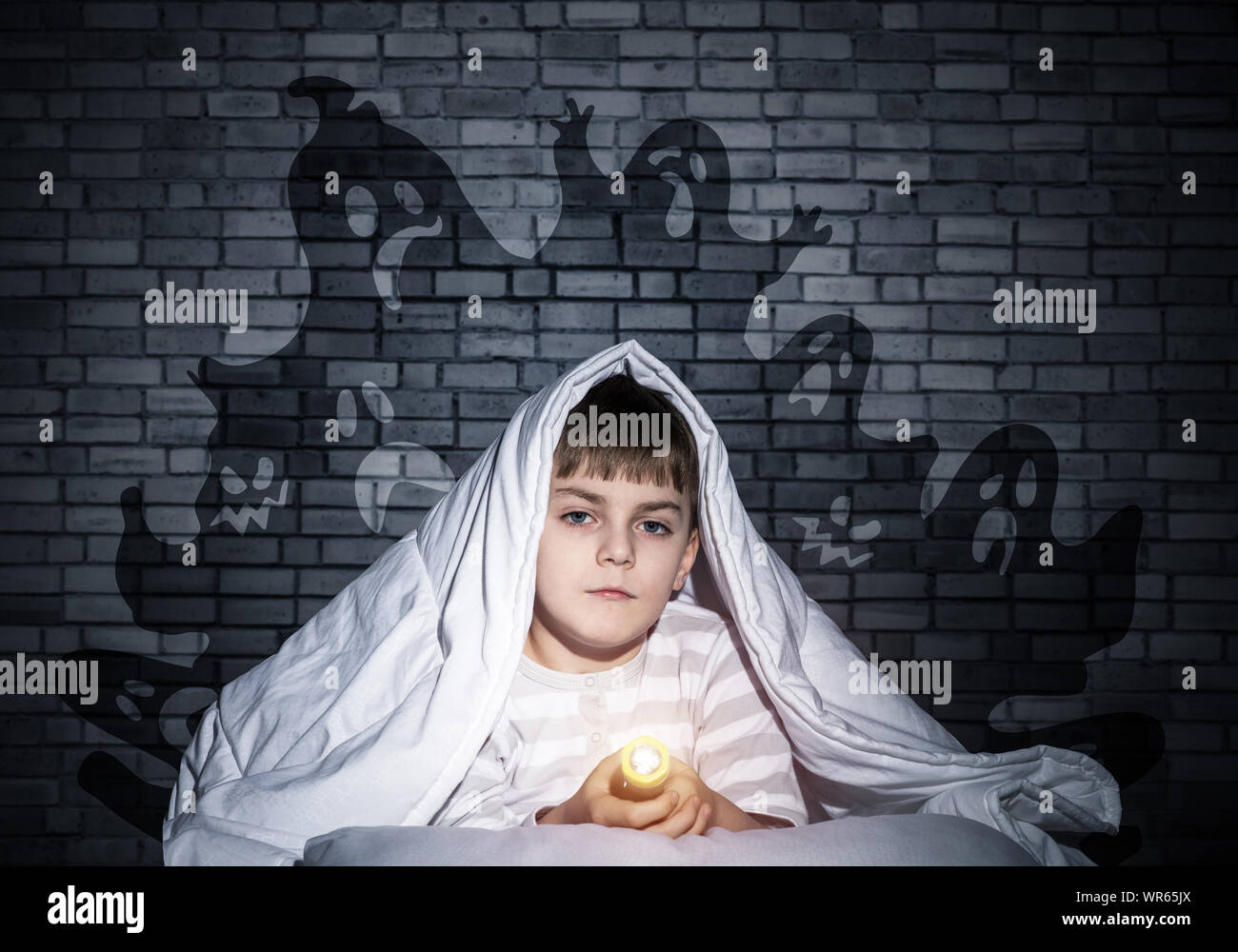 Serious child with flashlight hiding under blanket. Halloween scary ...
