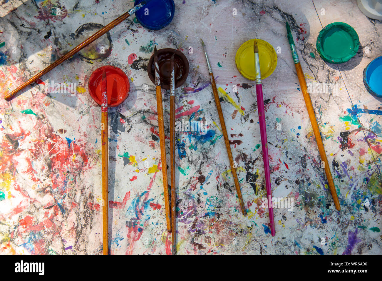Paintbrushes and paints on colorful messy tabletop Stock Photo - Alamy