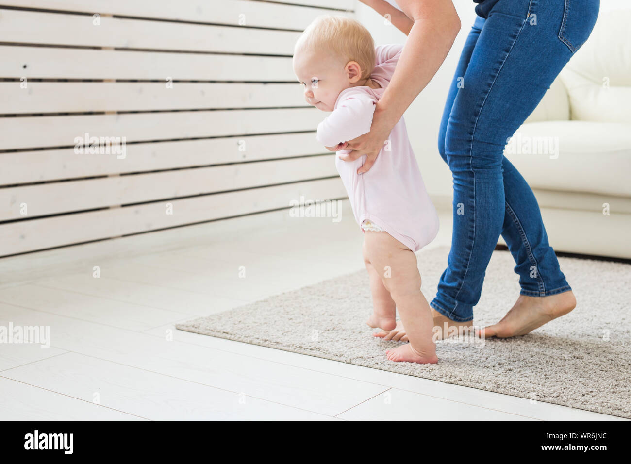 First steps of baby toddler learning to walk in white sunny living room ...