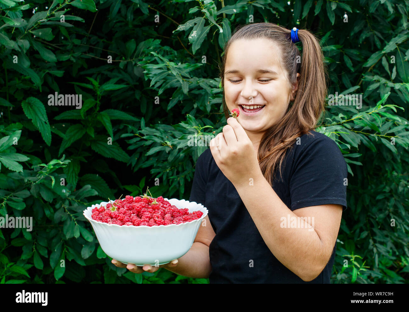 beautiful teen girl holding a bowl of raspberries in the garden closeup ...
