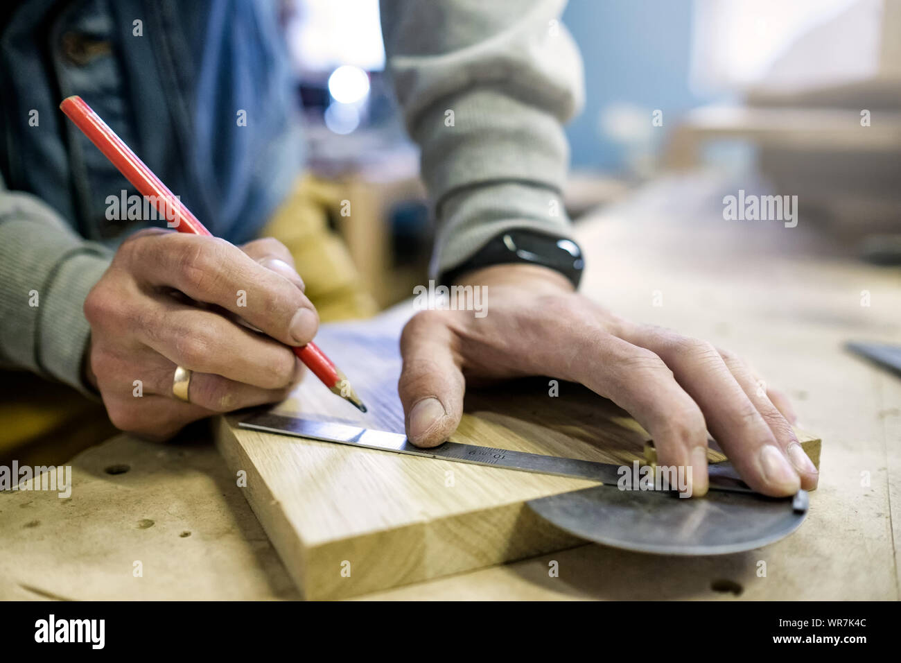 Carpenter using a straightedge to draw a line on a board marking a ...