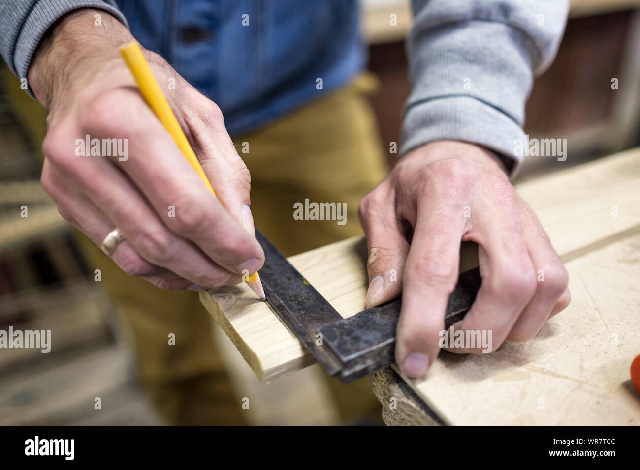 Carpenter using a straightedge to draw a line on a board marking a ...